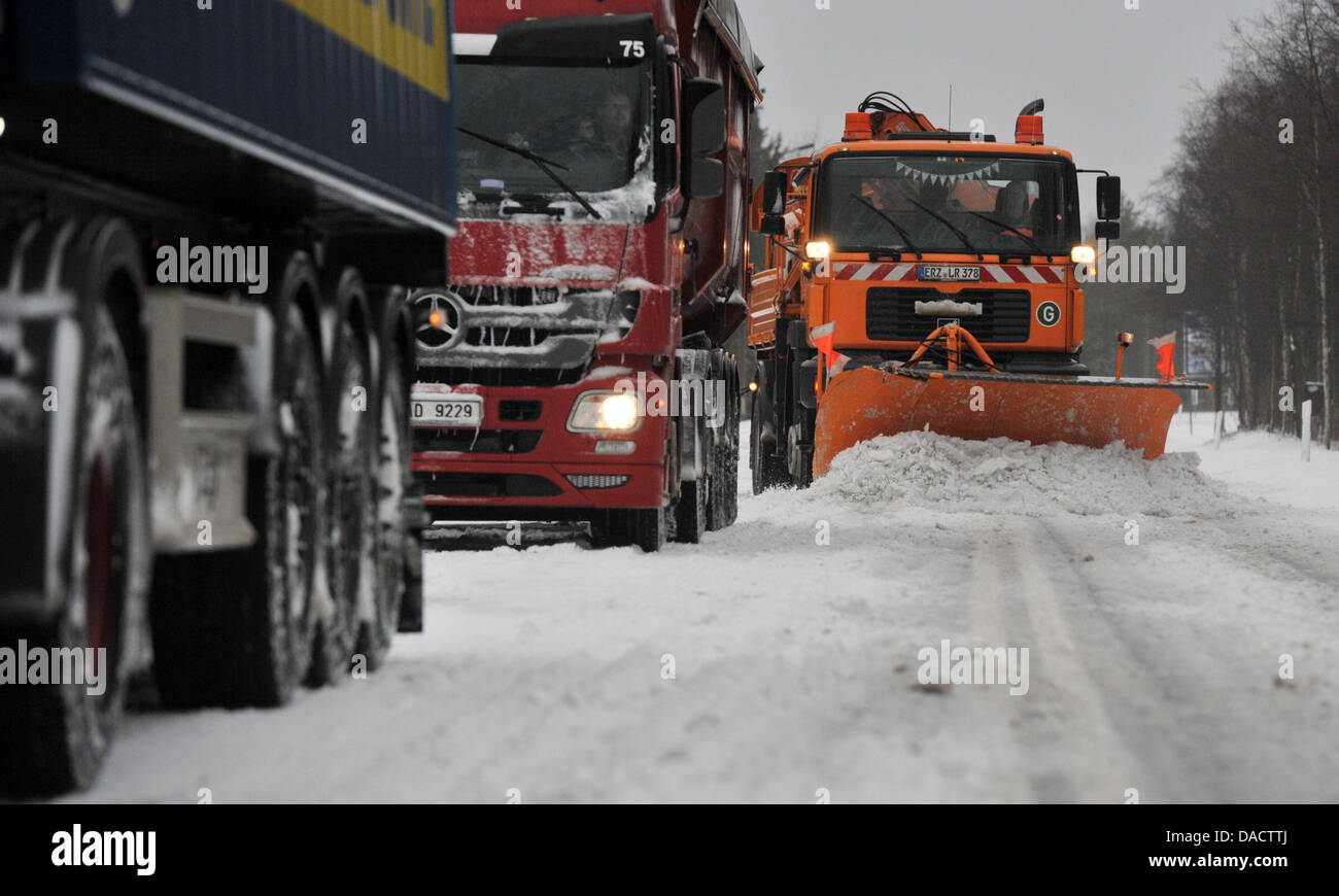 A snow plow cleans the roads next to a row of trucks at the ...