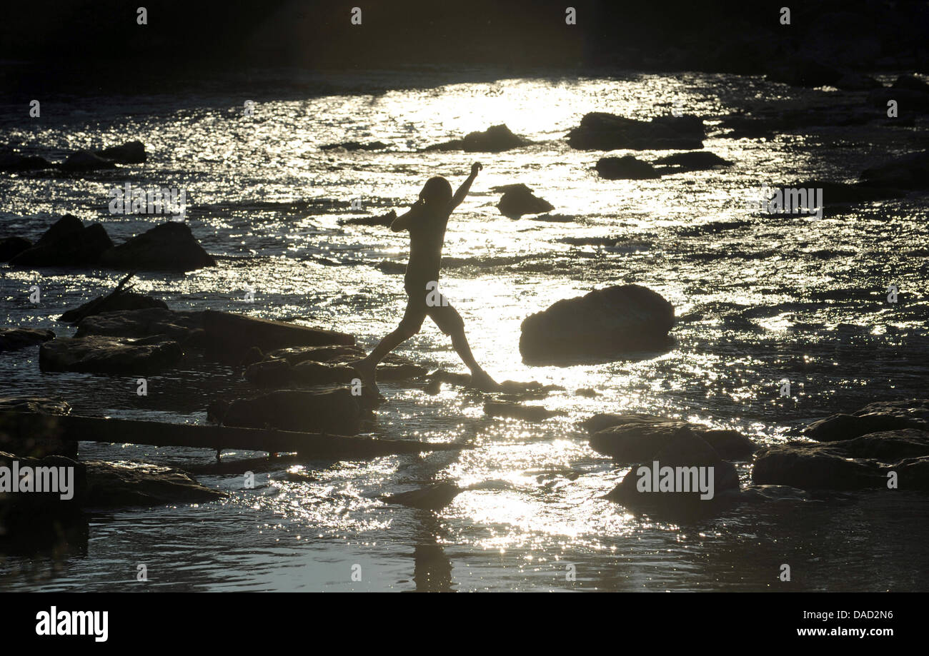 A boy enjoys the sun and jumps along rocks in the Isar in Munich ...