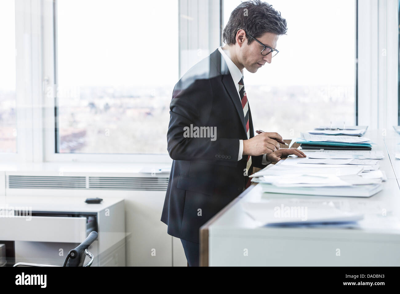 Businessman standing in office looking at paperwork Stock Photo - Alamy