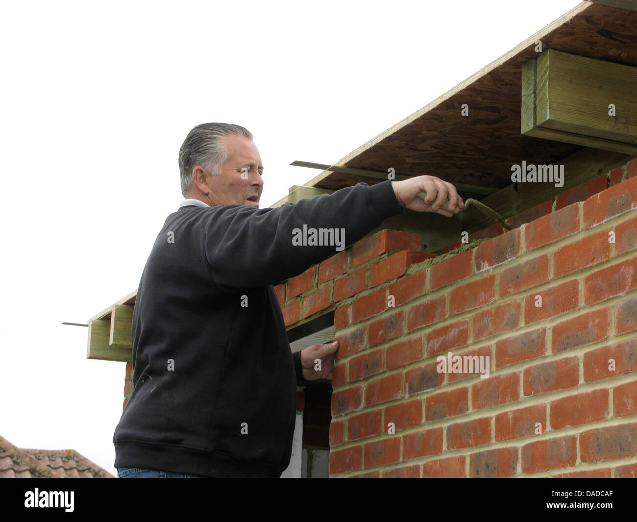 Builder / construction worker building a brick wall cementing bricks in ...