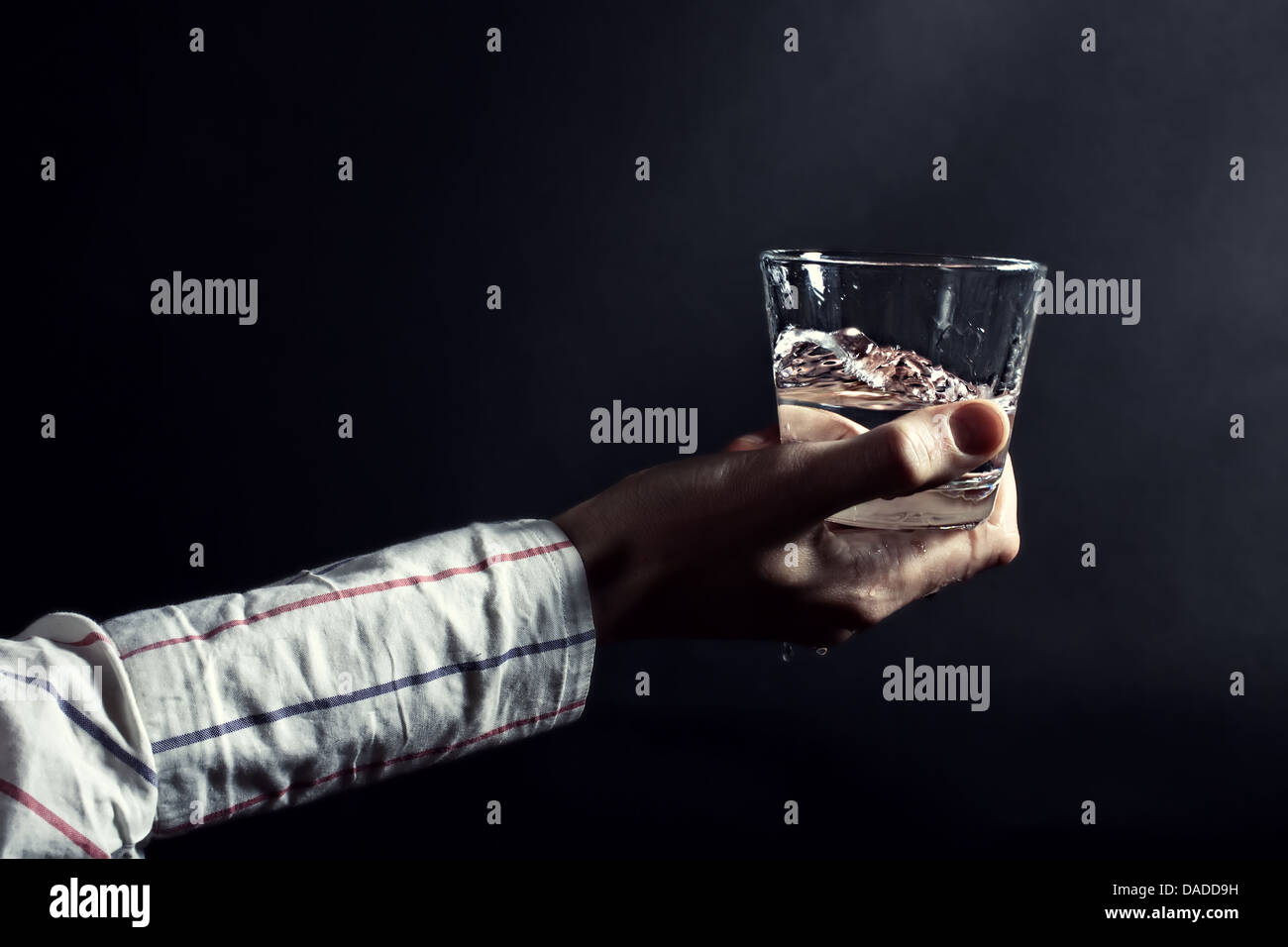 Hand holding a clear glass of water on a black background close up ...