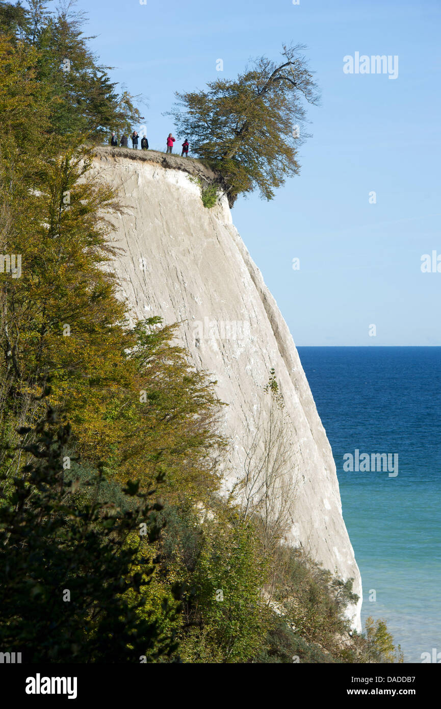 Tourists stand on the chalk cliffs under already green and red coloured ...