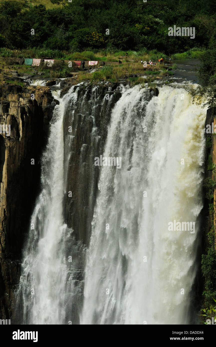 View of water cascading over waterfall edge next to locals washing ...