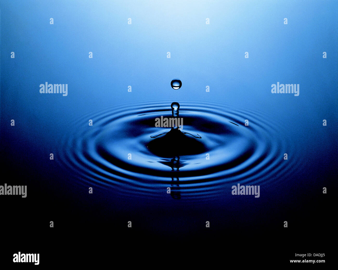 This close-up image captures a single drop of water falling, creating ...