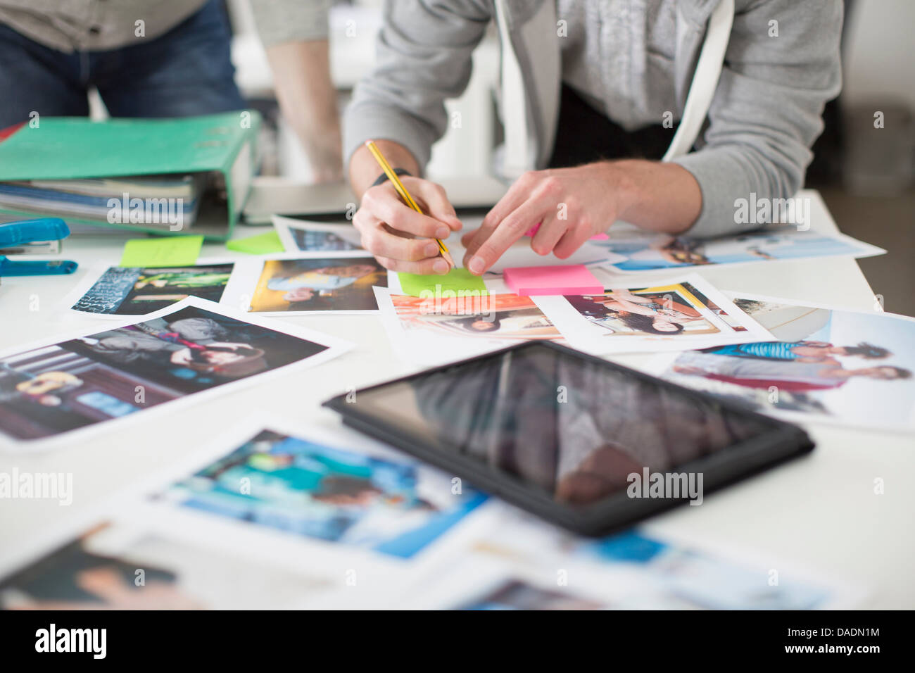 Young man making notes on desk of photographs with digital tablet in ...