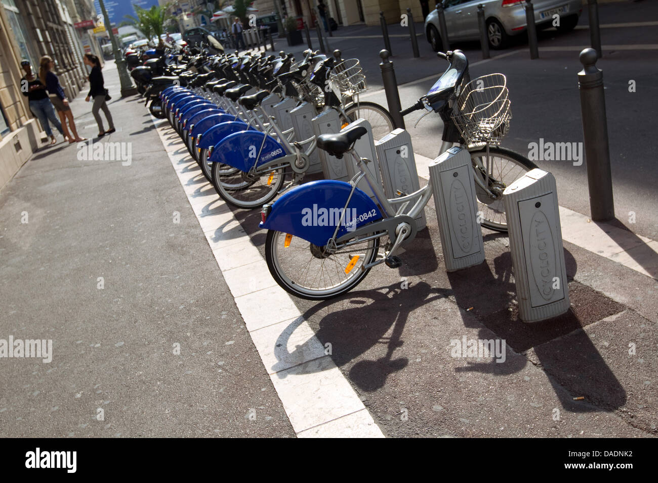 A group of people stand next to a line of rentable velo bicycles in ...