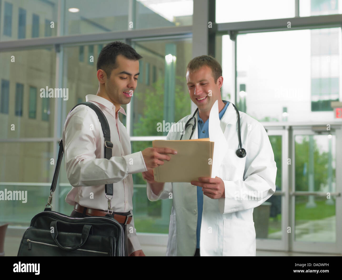 Doctor looking at file with mid adult man, smiling Stock Photo - Alamy