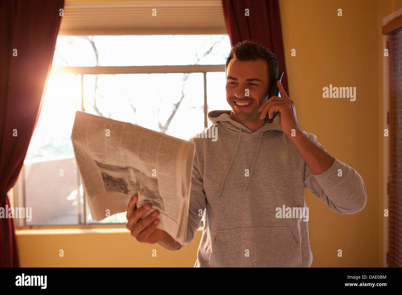 Young man looking at newspaper and using mobile phone in hotel room ...
