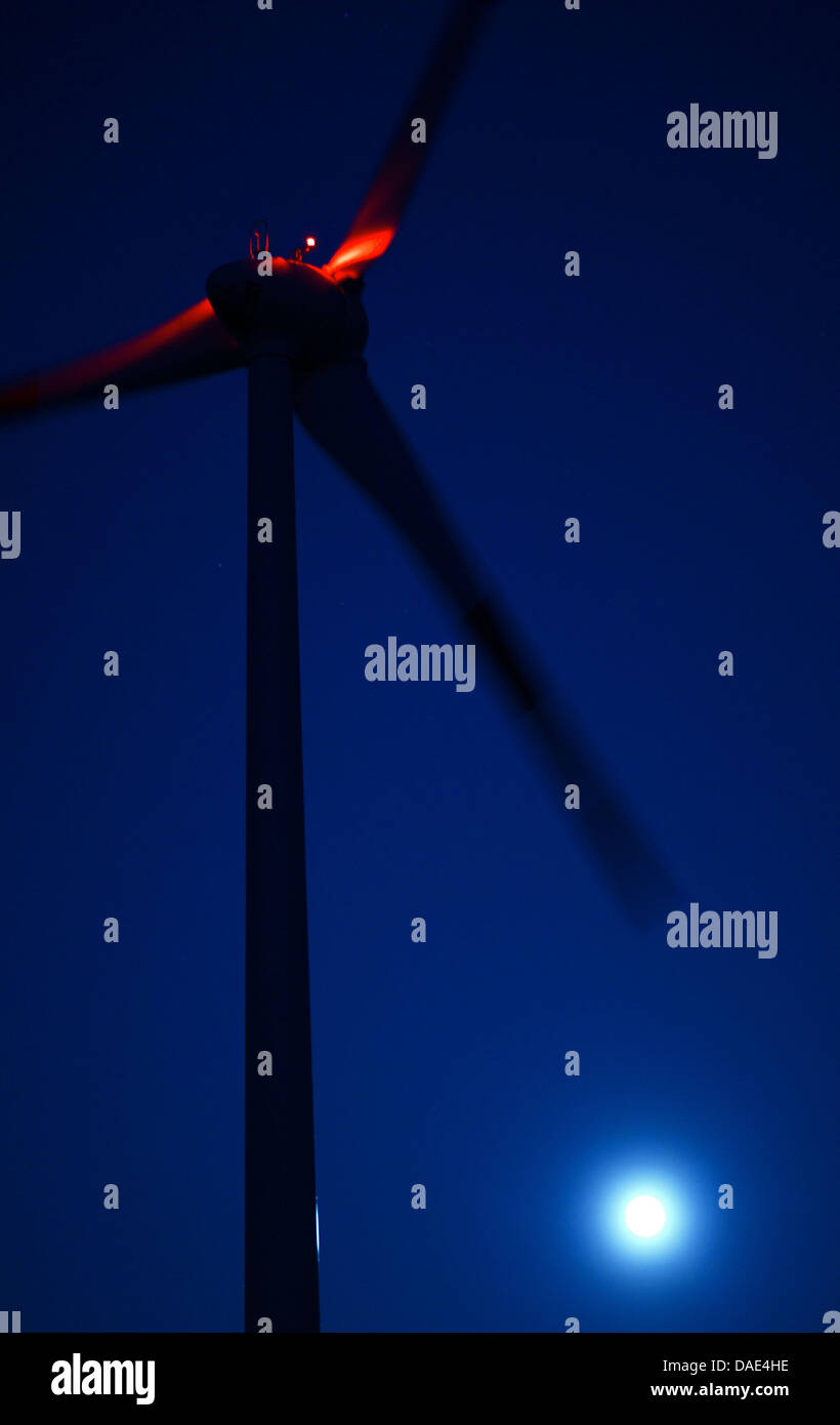 A wind turbine with a red marker light turns in a wind park near ...