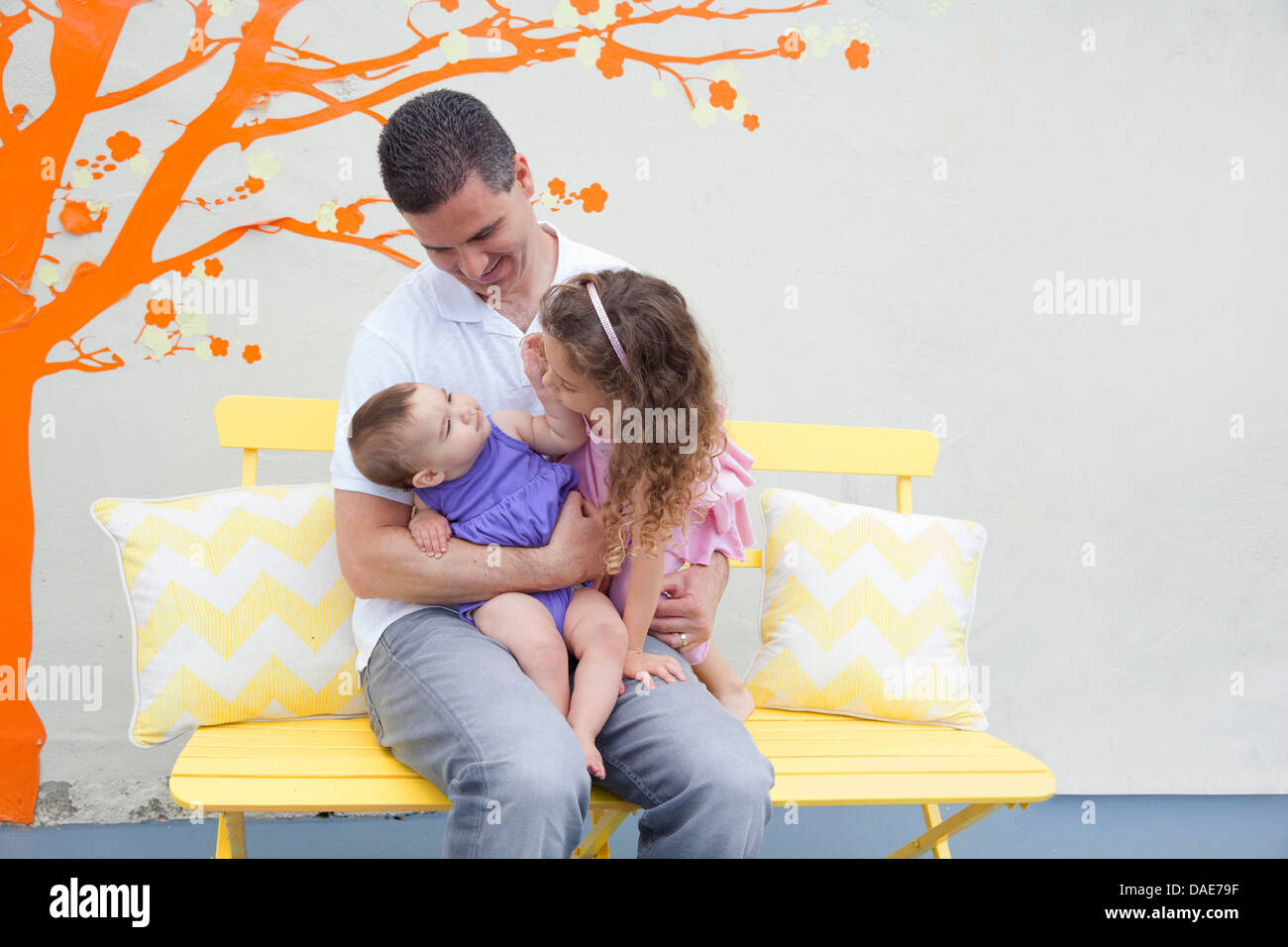Father sitting on bench with two daughters on lap Stock Photo - Alamy