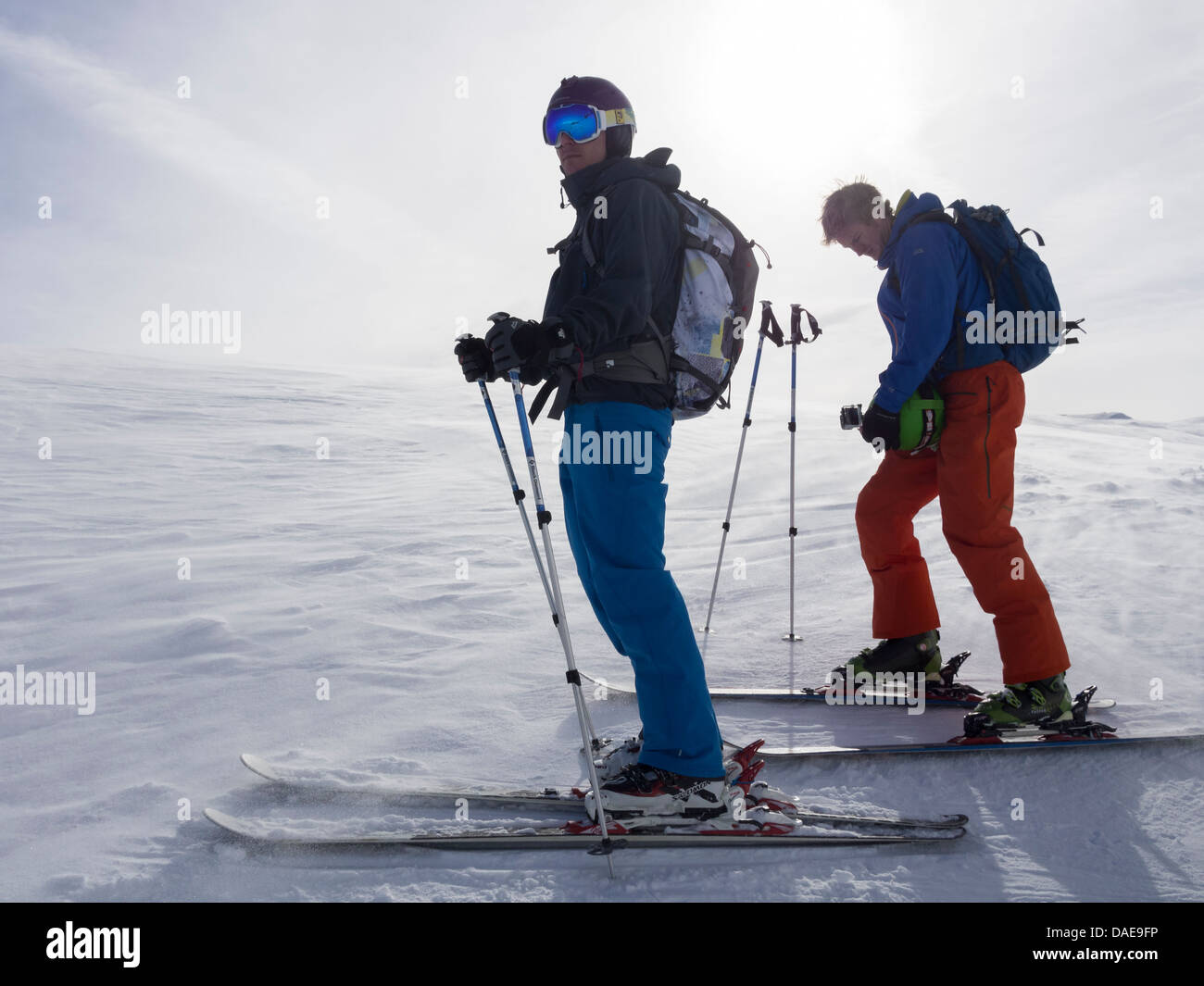 Two male skiers on skiing holiday backlit against sun on snow slopes in ...