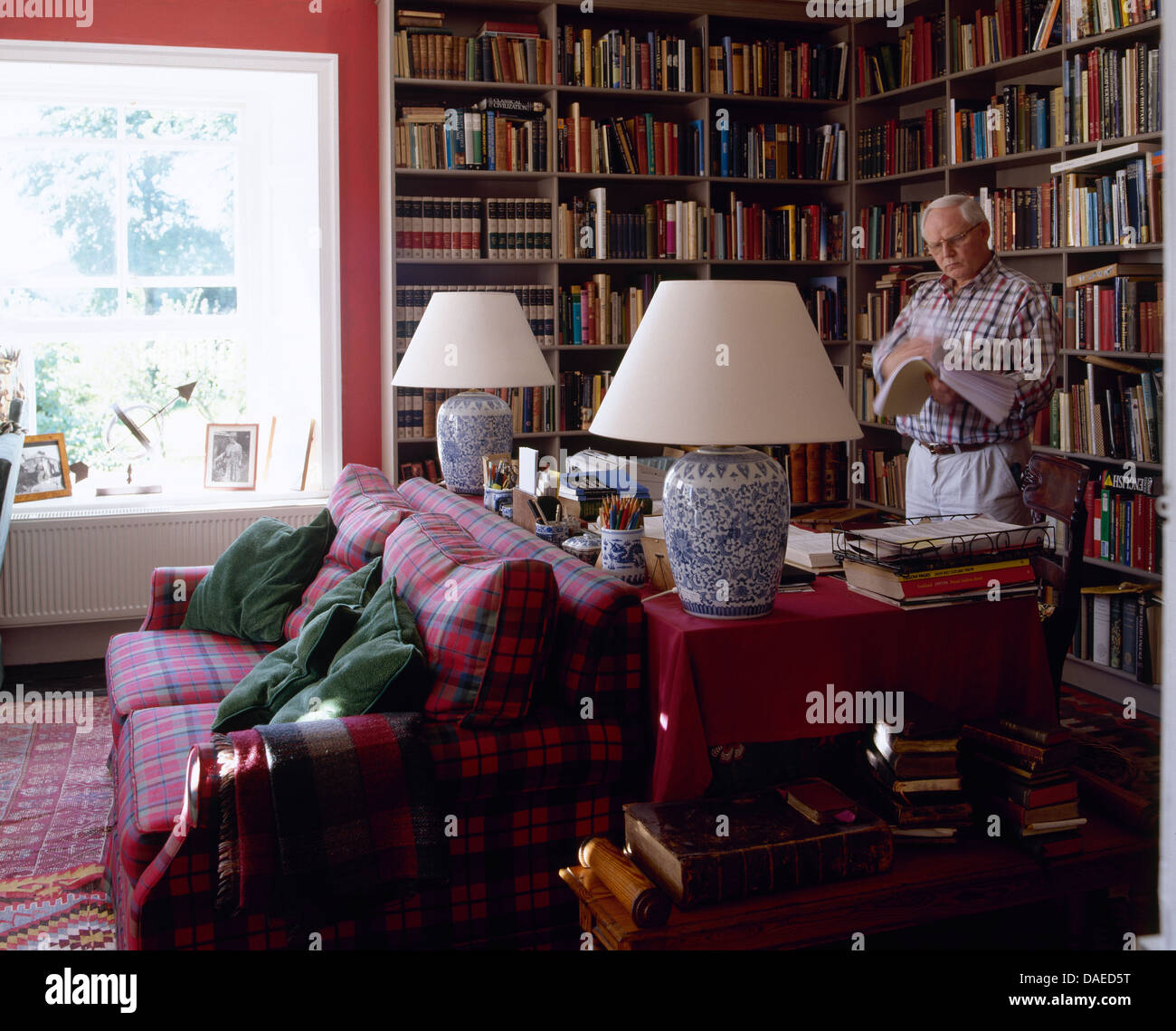 Middle-aged man standing and reading in front of bookcase in country ...