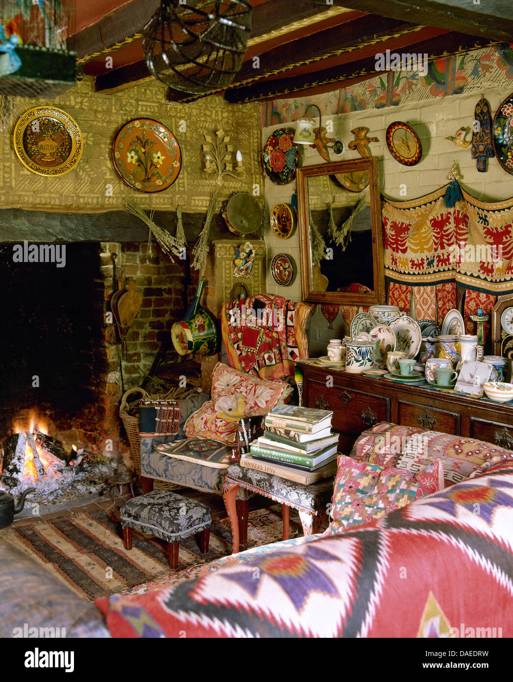 Lighted fire in fireplace in cluttered cottage living room with Indian ...
