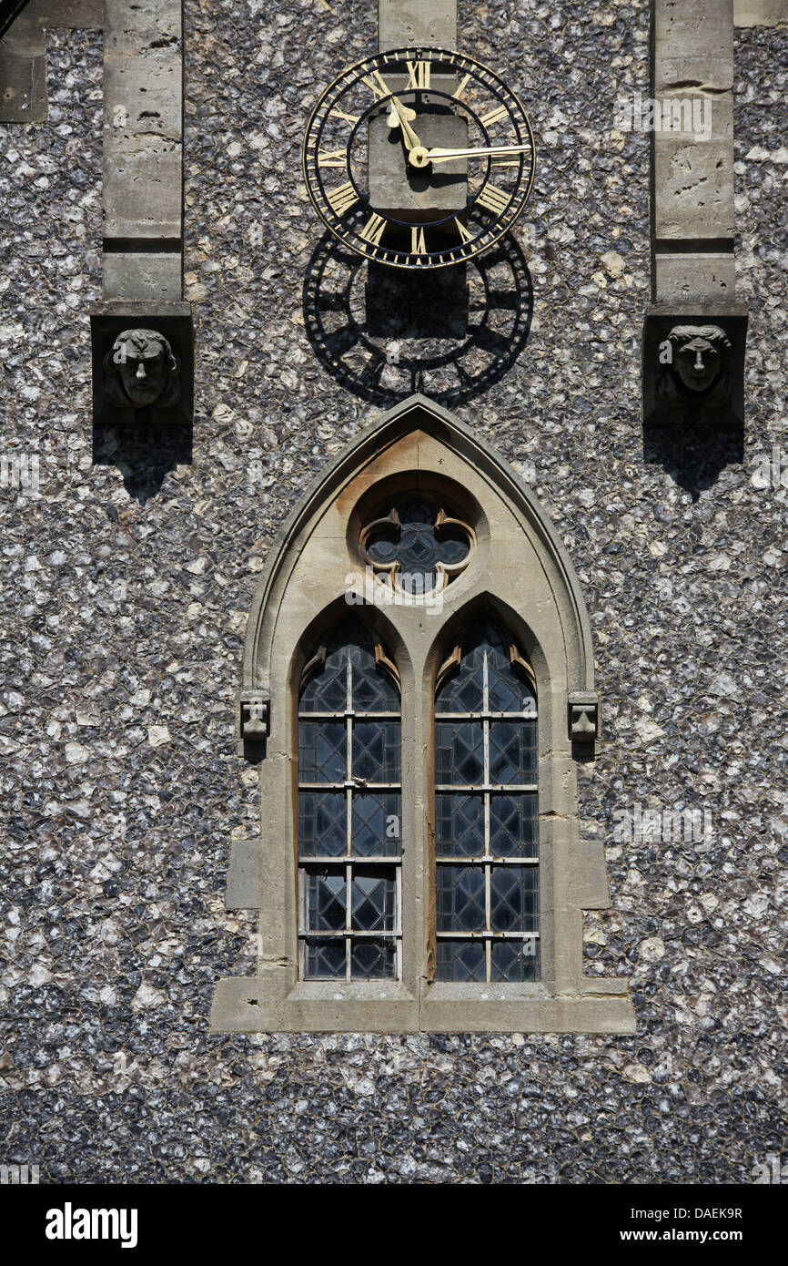 A large clock on a church building with a lead glass window below and ...