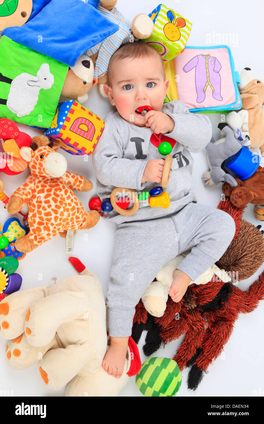 baby lying beween playthings in supine position and sucking at a toy ...