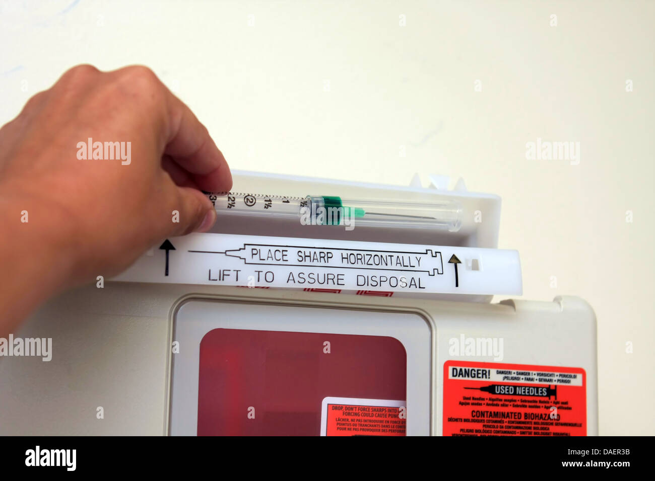 nurse hand placing used needle syringe into red sharps biohazard ...
