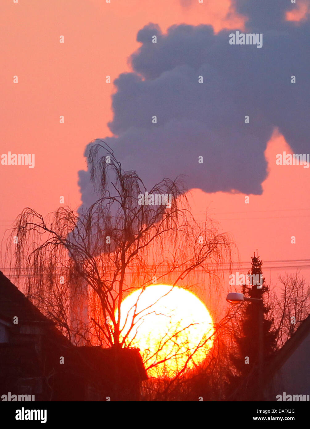 A glowing red sun sets between houses and a heat and power station at ...