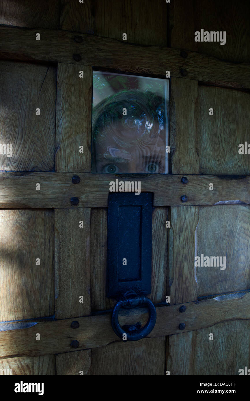 Terror, girl looking through the glass of a front door Stock Photo - Alamy