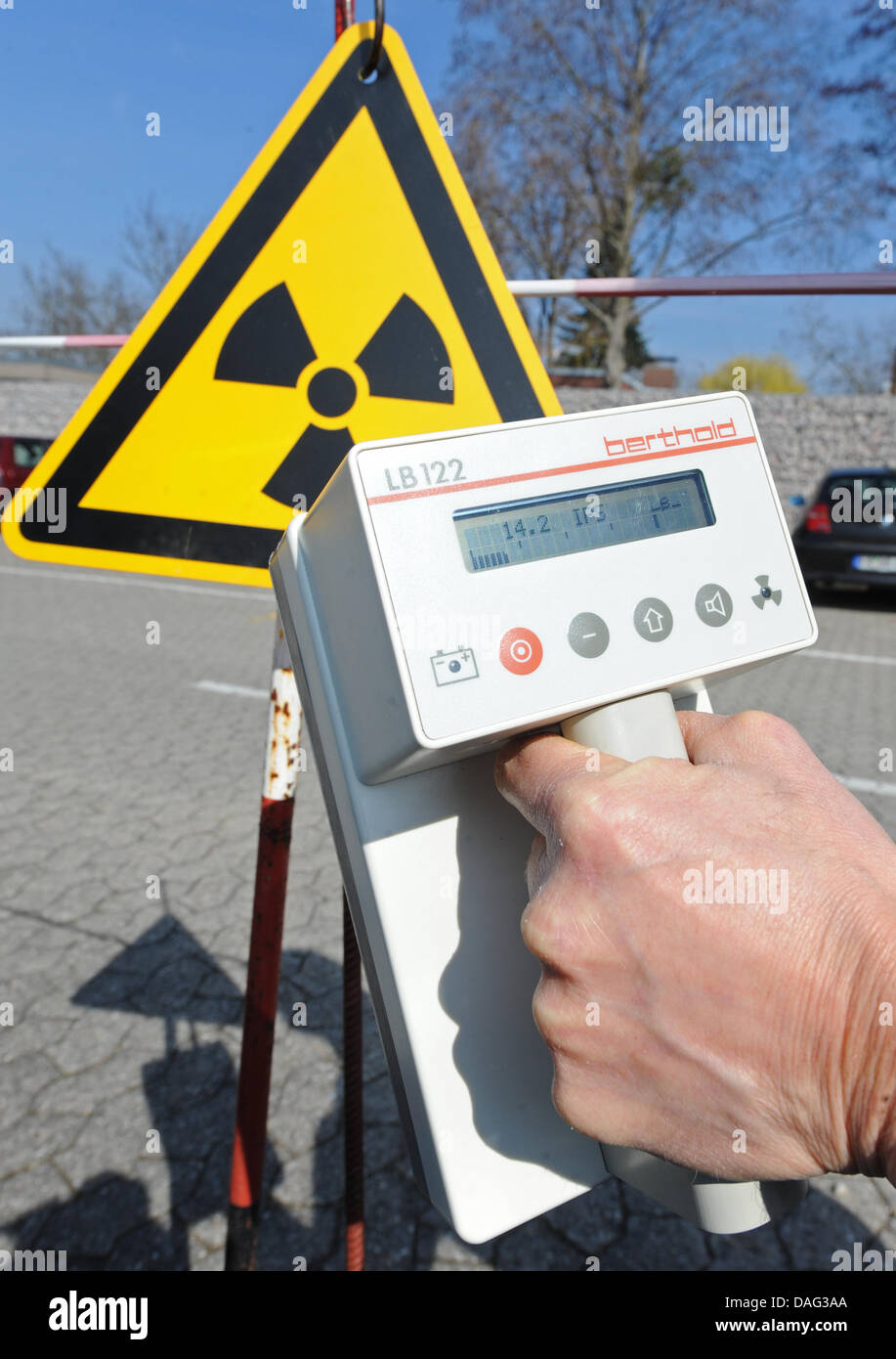 A Geiger counter is held in front of a sign warning from radioactivity ...