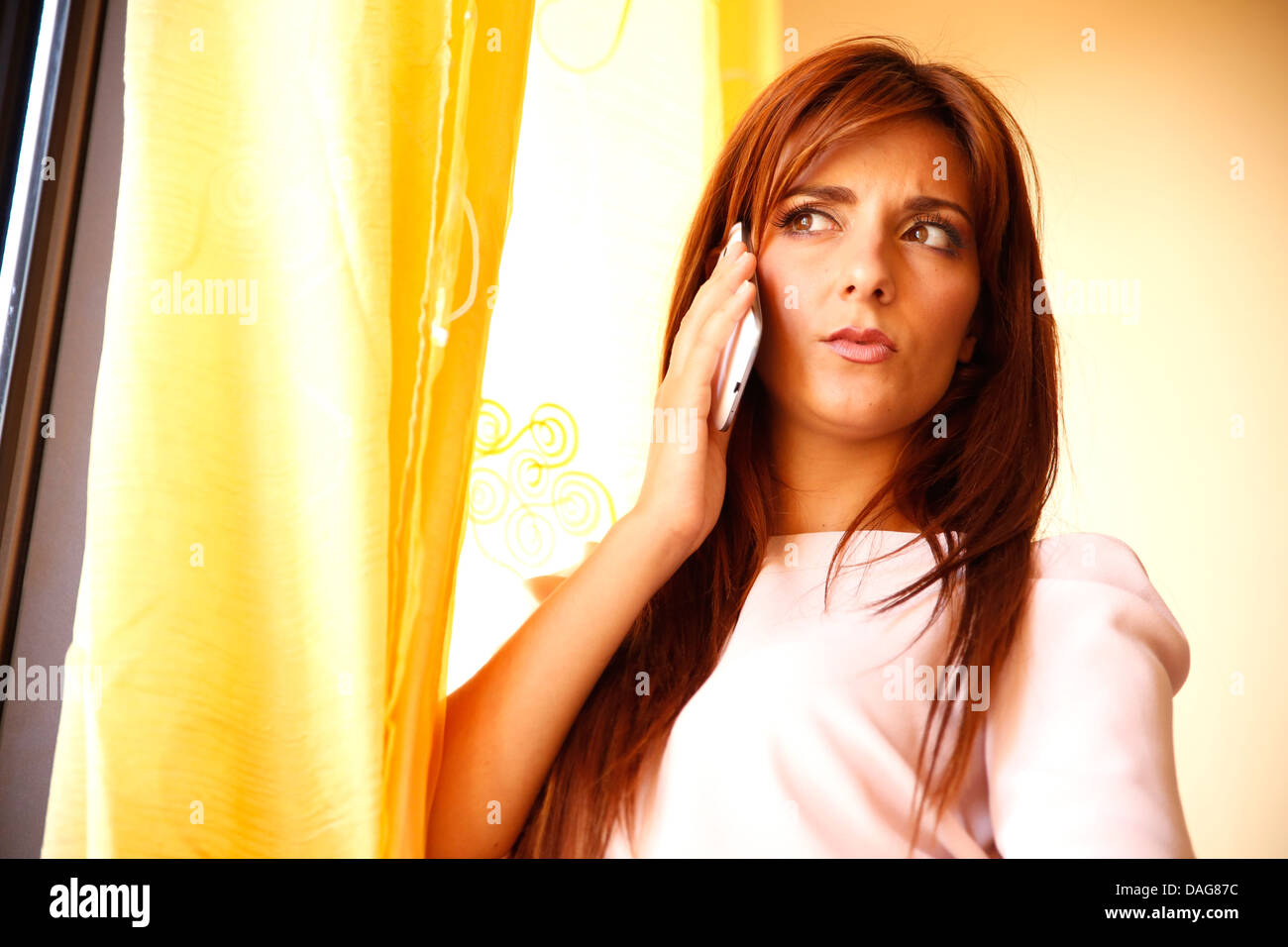 A beautiful woman waiting at the window while talking on the phone ...