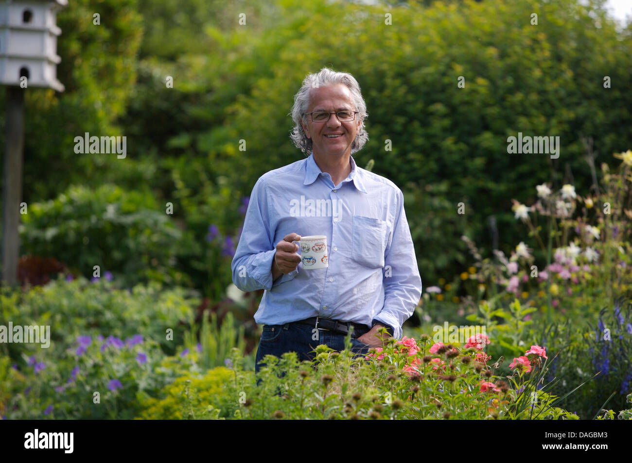 Portrait of a smiling man standing with a cup of tea in the garden ...