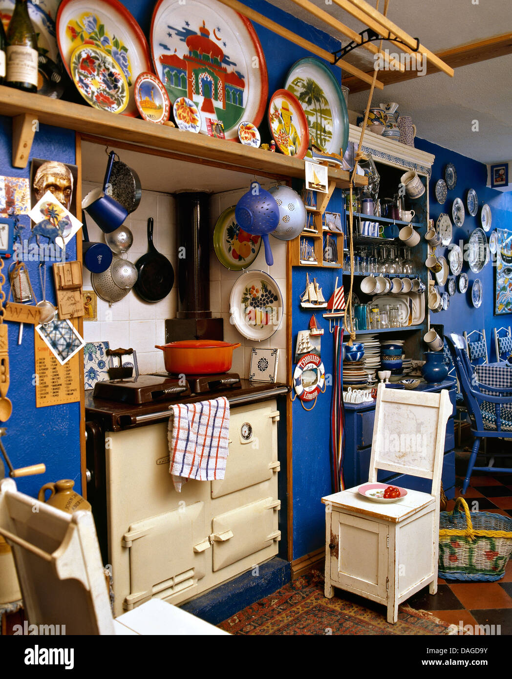 Shelf with row of colorful plates above cream Aga in cluttered blue ...