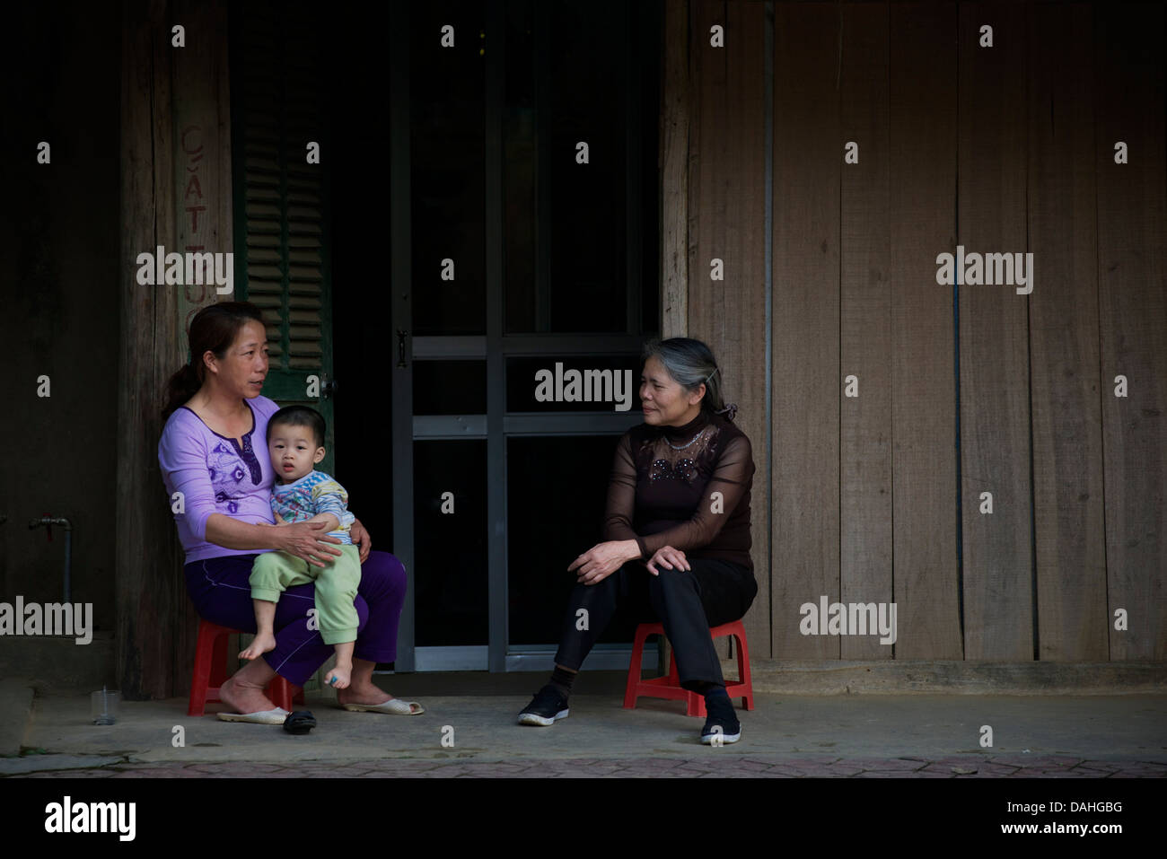 Vietnamese mother, grandmother and child relaxing outside their home ...
