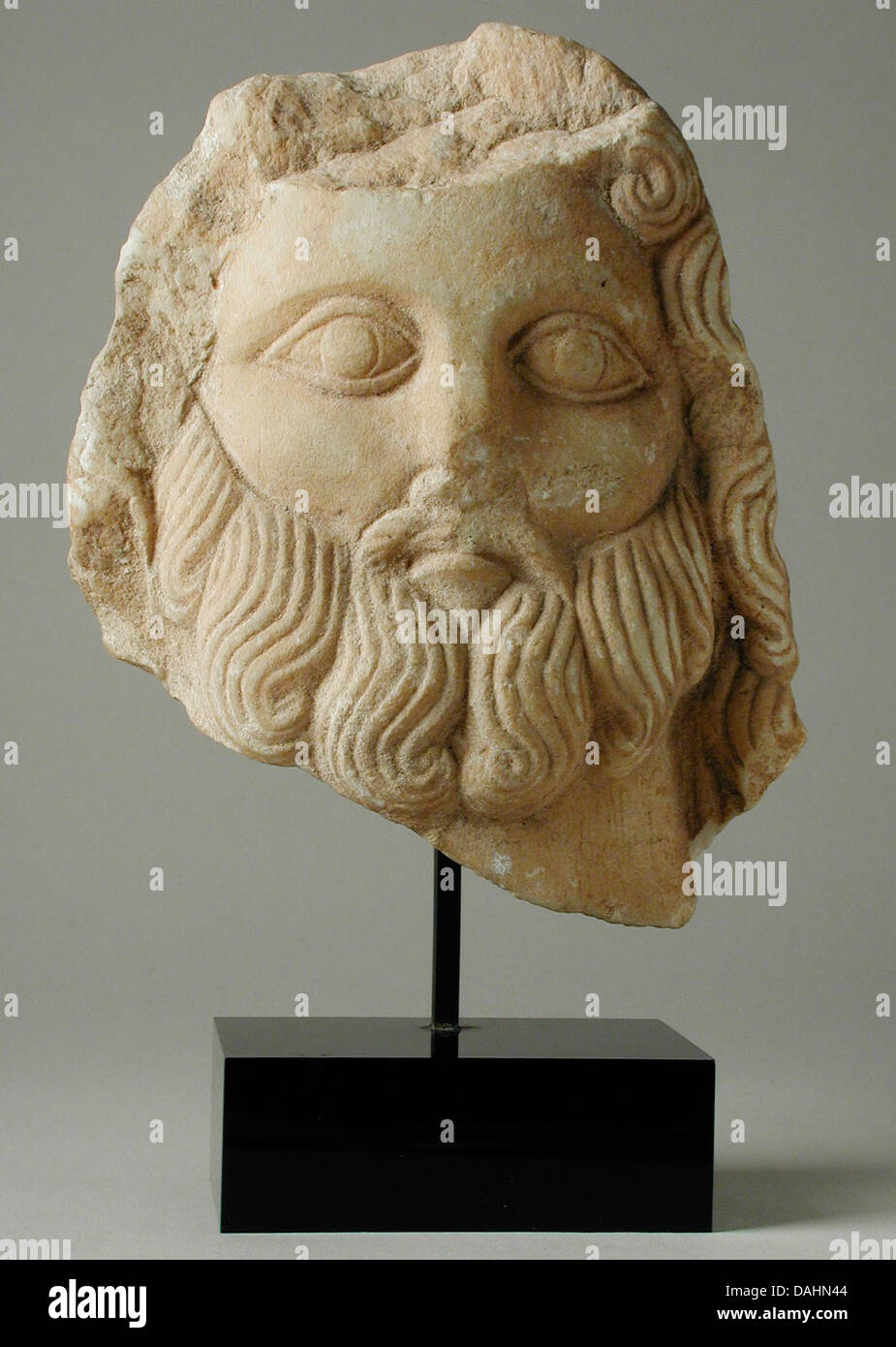 This ancient sculpture presents the head of a male figure, showcasing ...