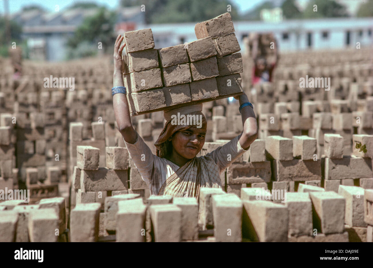 A female labourer carrying baked bricks on her head in a brick factory ...