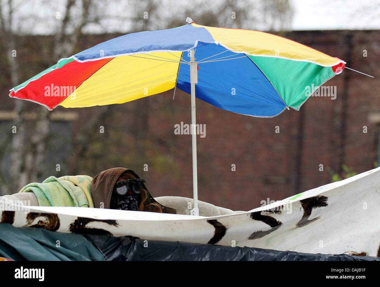 A mummed person sits underneath an umbrella on barricades situated in ...