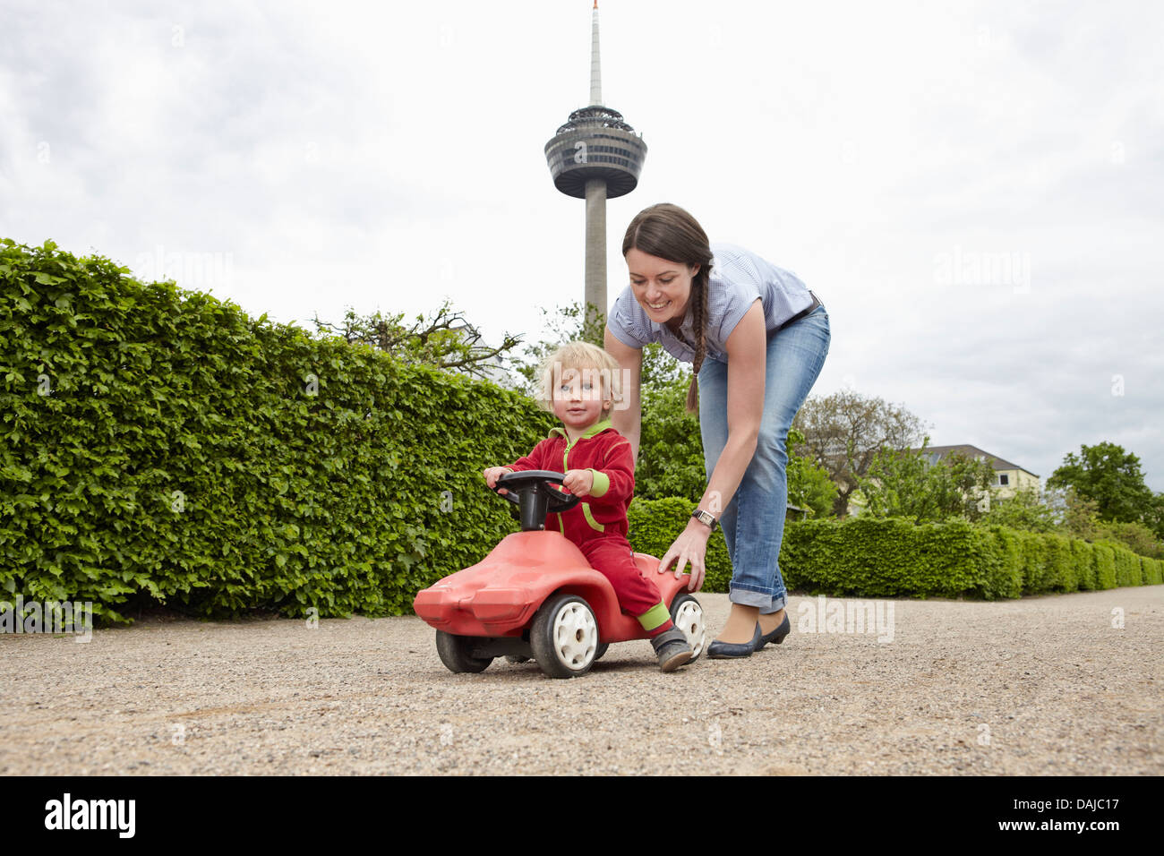 Germany, Cologne, Mother carrying daughter in toy car, smiling Stock ...