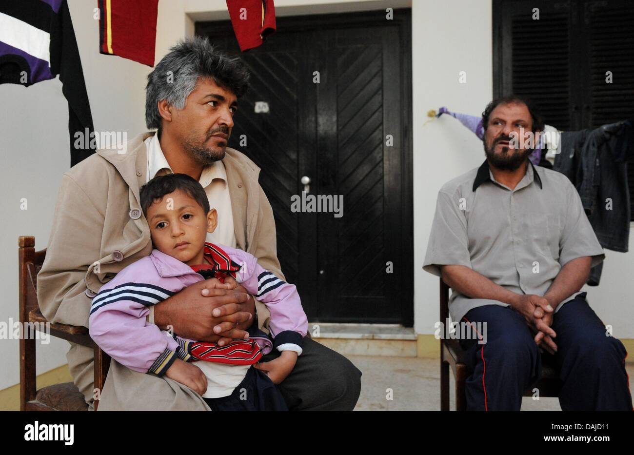 A father sits with his son on his lap (L) in front of a cottage of a ...