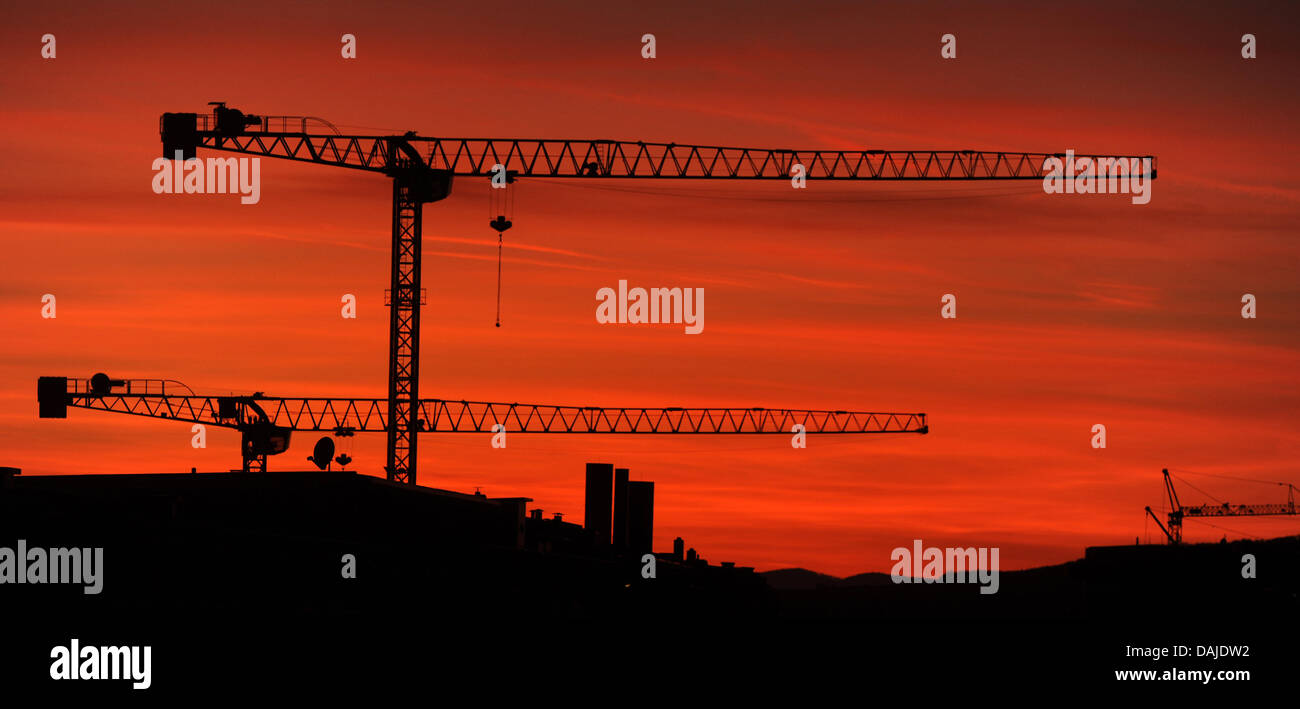 Three construction cranes stand tall in front of backdrop of a blazing ...
