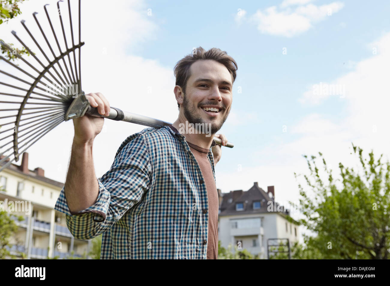 Germany, Cologne, Portrait of young man holding rake, smiling Stock ...