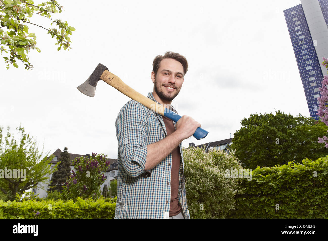 Germany, Cologne, Portrait of young man holding axe, smiling Stock ...