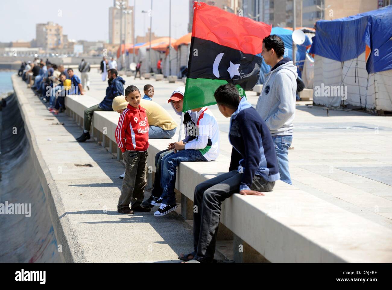 Young Libyans cary the Libyan flag as they sit on a bench looking out ...