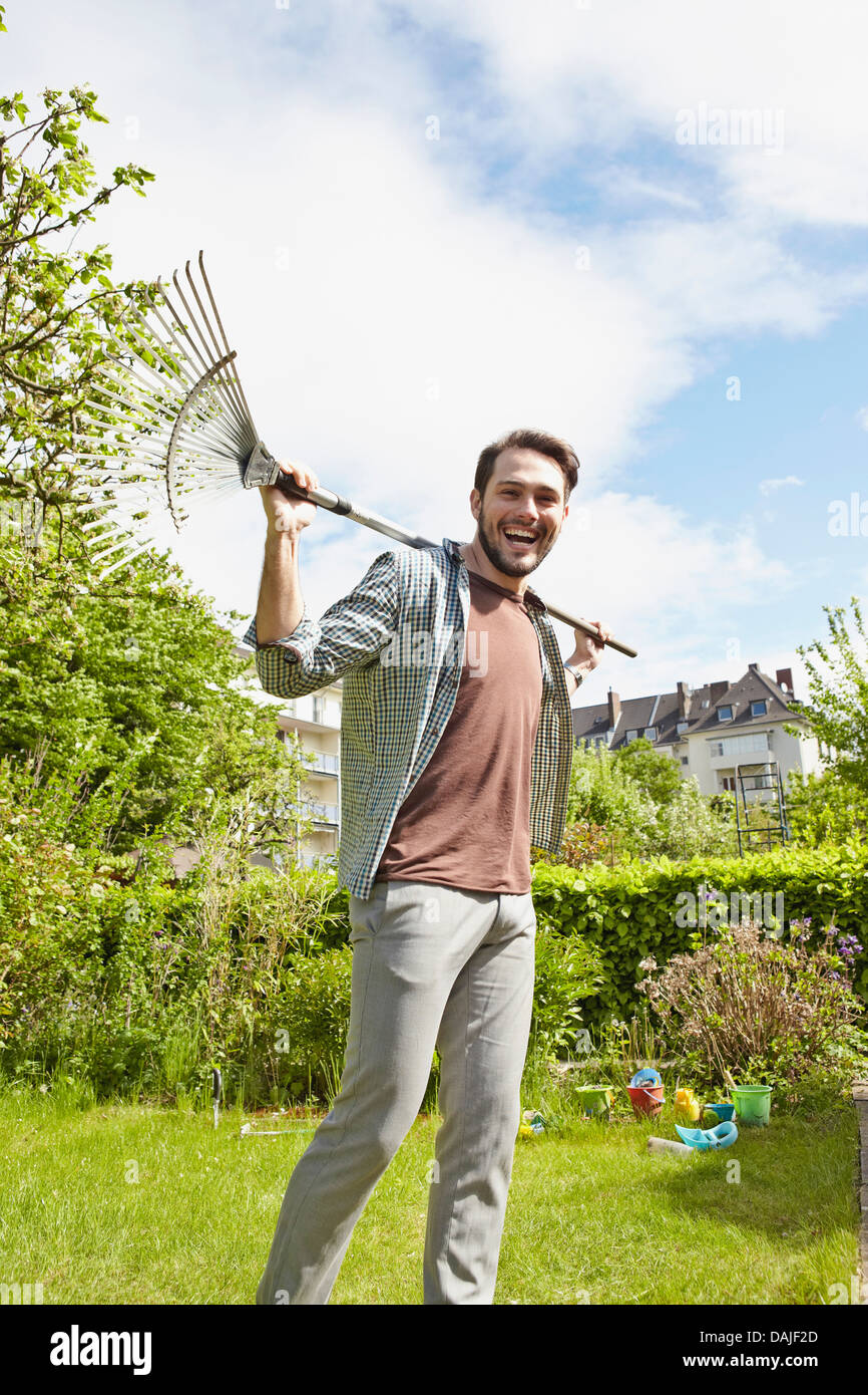 Germany, Cologne, Portrait of young man holding rake, smiling Stock ...