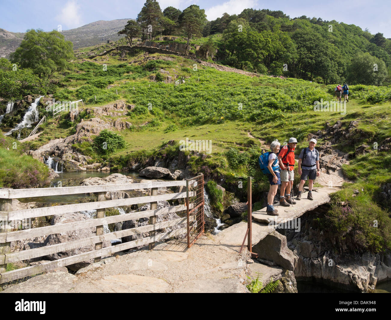 Walkers crossing old stone footbridge over Afon Cwm Llan river on path ...