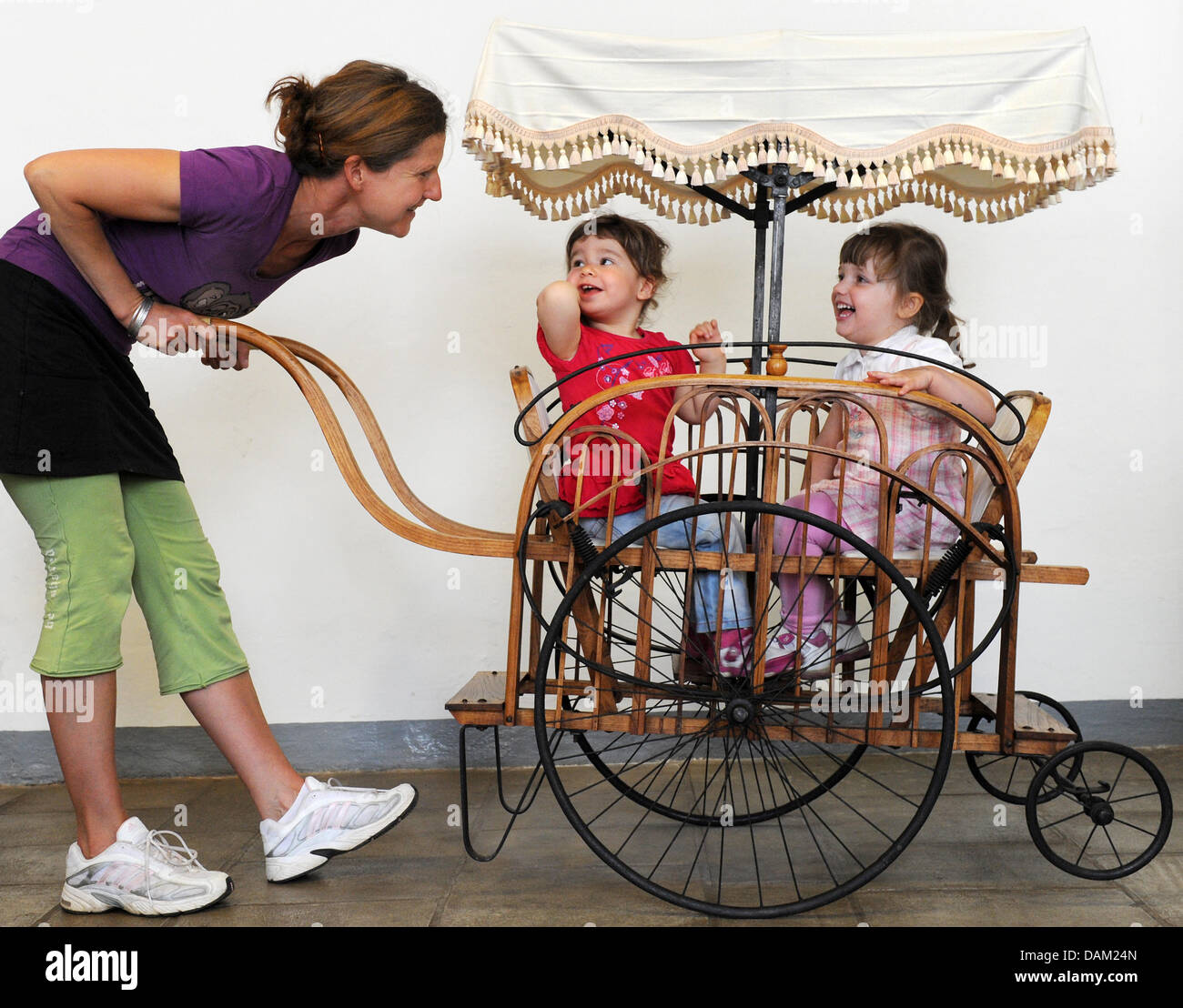 Two-year-old Lena and Naila sit inside a wooden stroller from around ...