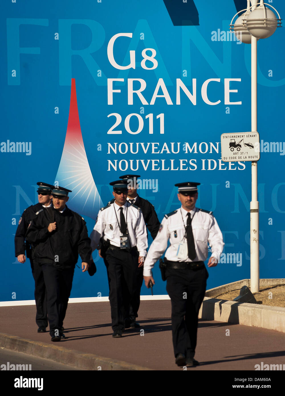 Police officers walk past a poster of the G8 summit in Deauville ...