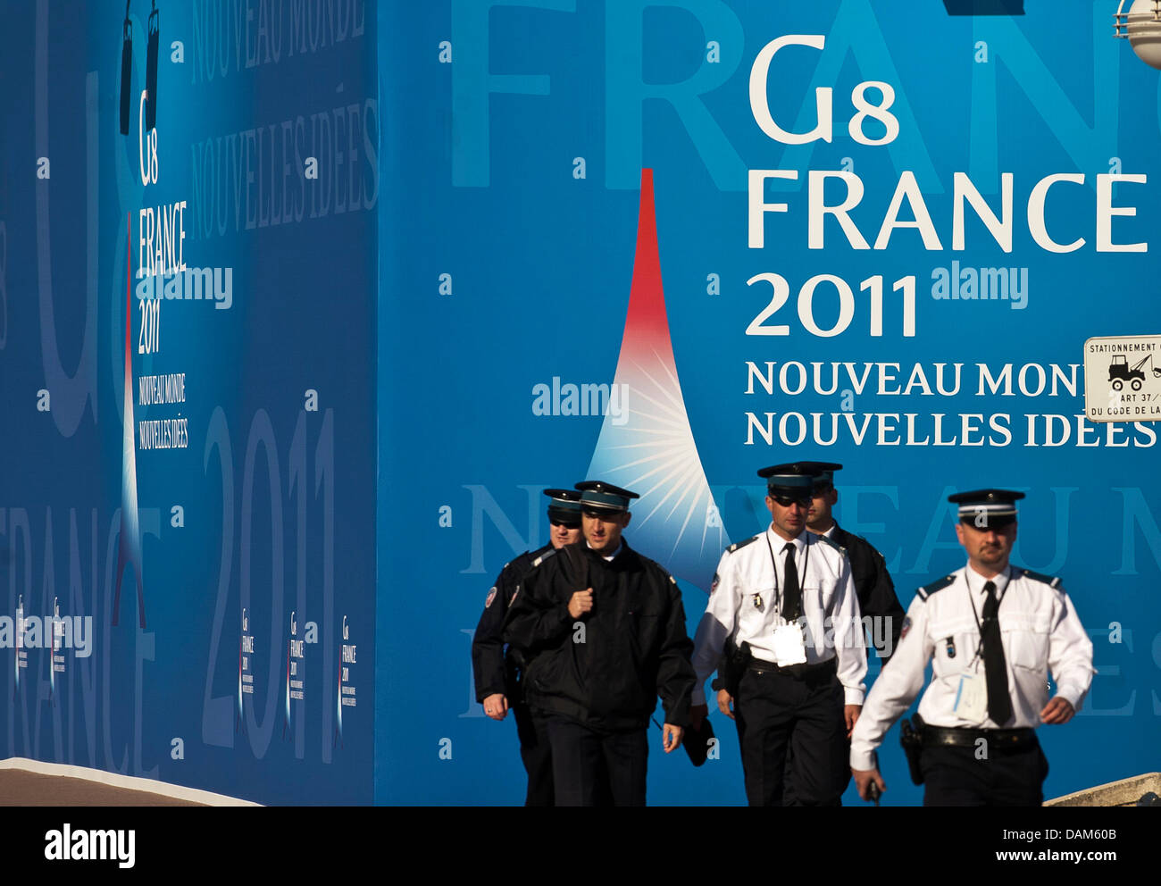 Police officers walk past a poster of the G8 summit in Deauville ...