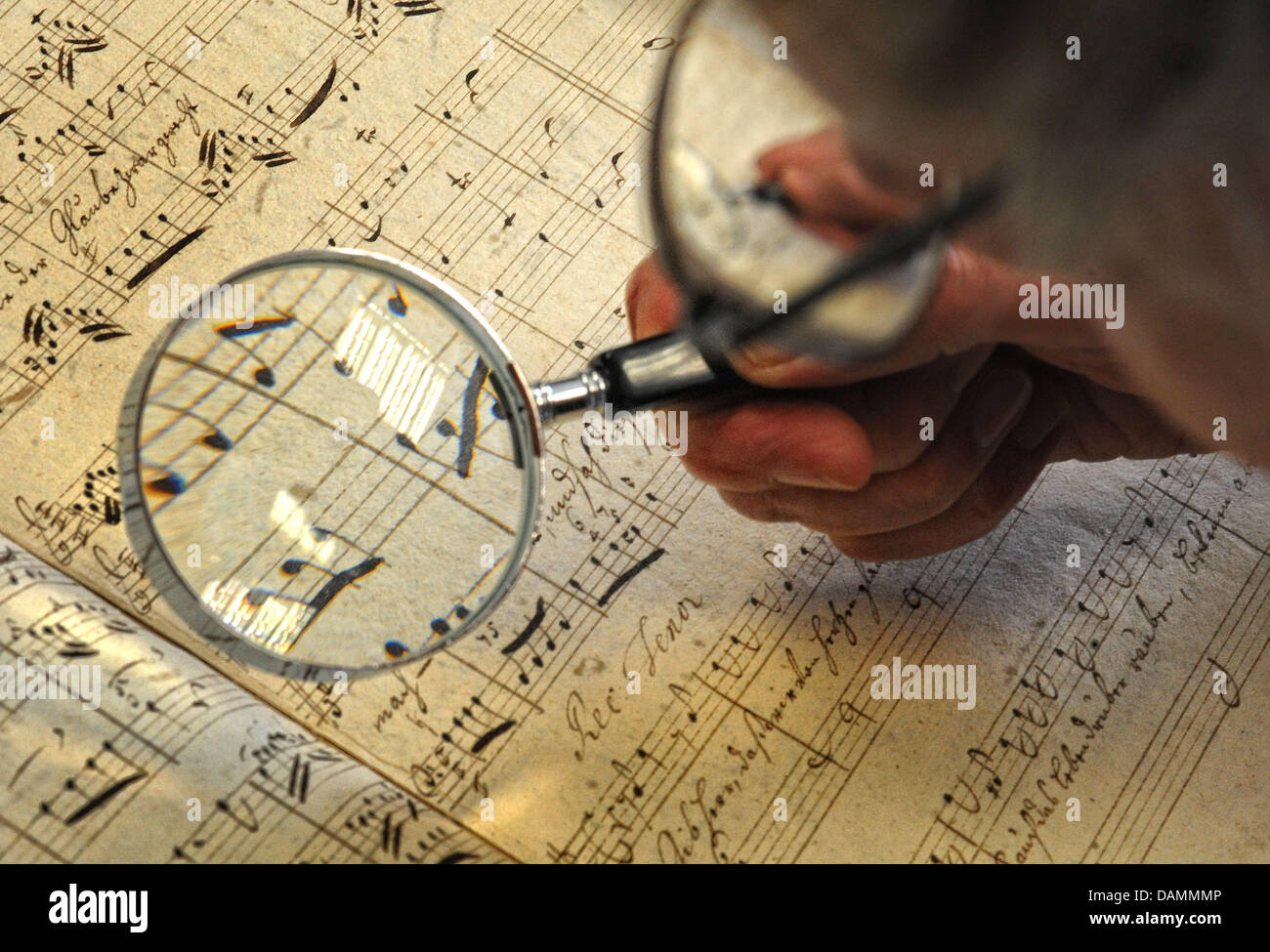 A scientist uses a magnifying glass to study historical sheets of music ...