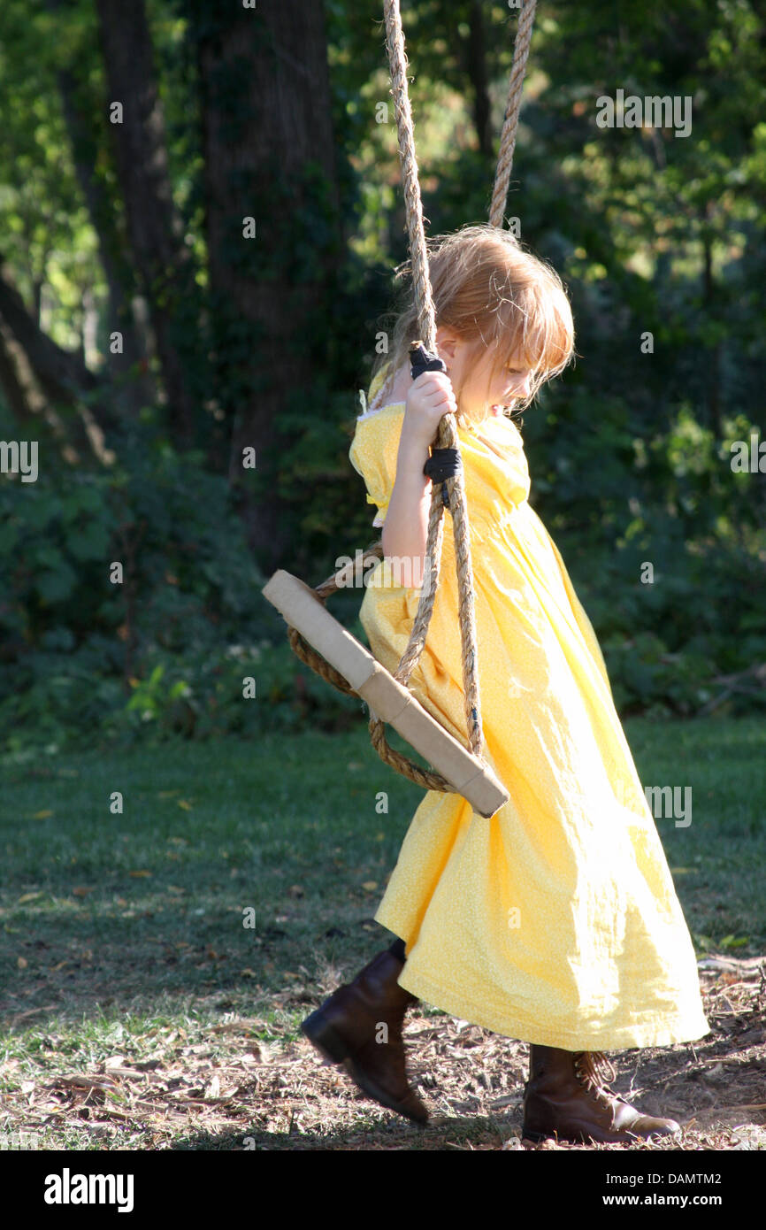 Young girl in a prairie dress getting on a rope swing Stock Photo - Alamy