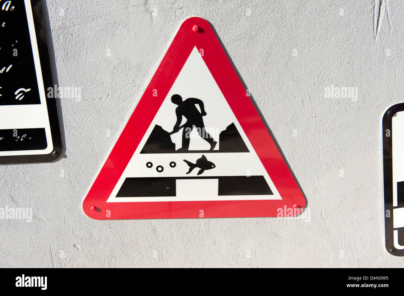 Sign Man digging up road fish in sewer pipe below Stock Photo - Alamy