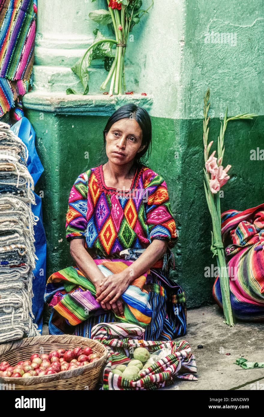 A K'iche' Maya woman with a sad expression selling fruits and flowers ...