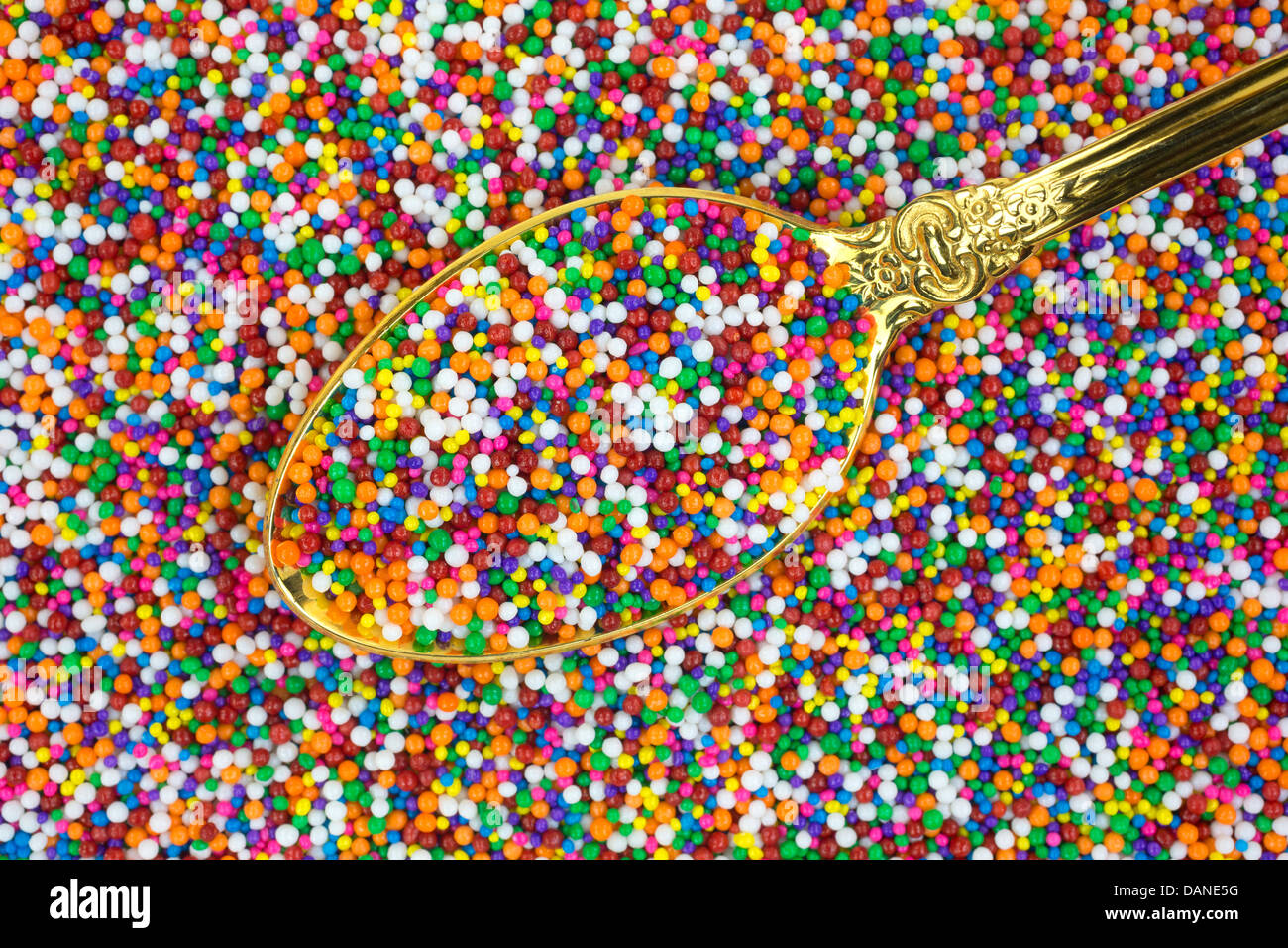 A very close view of a gold spoon filled with candy sprinkles atop a ...