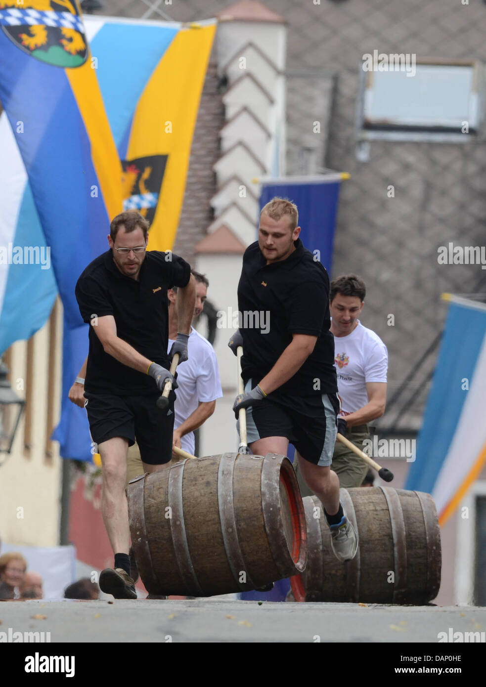 Two men use wooden sticks to roll a beer barrel through the streets ...