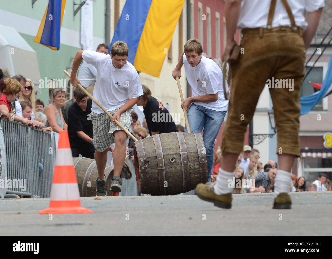 Two men use wooden sticks to roll a beer barrel through the streets ...