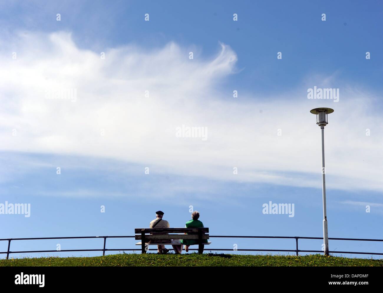 Visitors sit in the sun on a bench on the North Sea dyke in Buesum ...