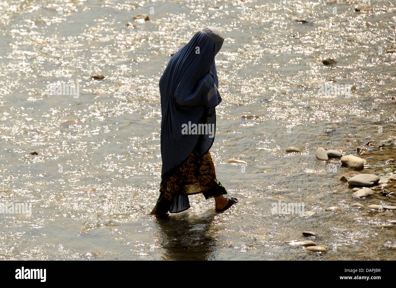 An Afghan woman walks along a river wearing a burka in Khanabad, near ...
